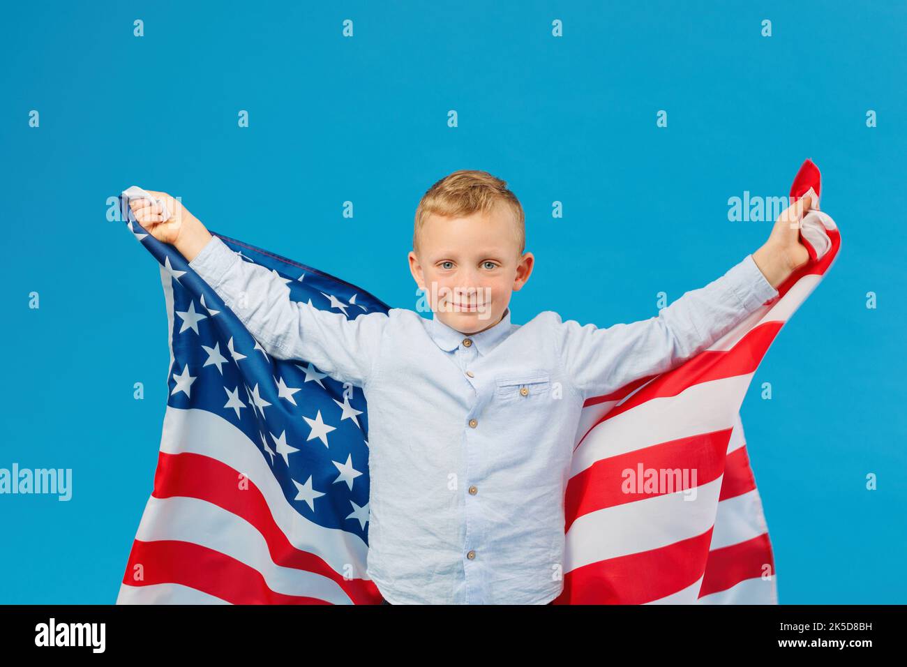 Cute boy holding American flag in indoor studio on blue background. The ...