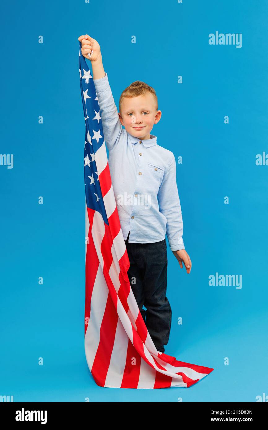 Cute boy holding American flag in indoor studio on blue background. The ...