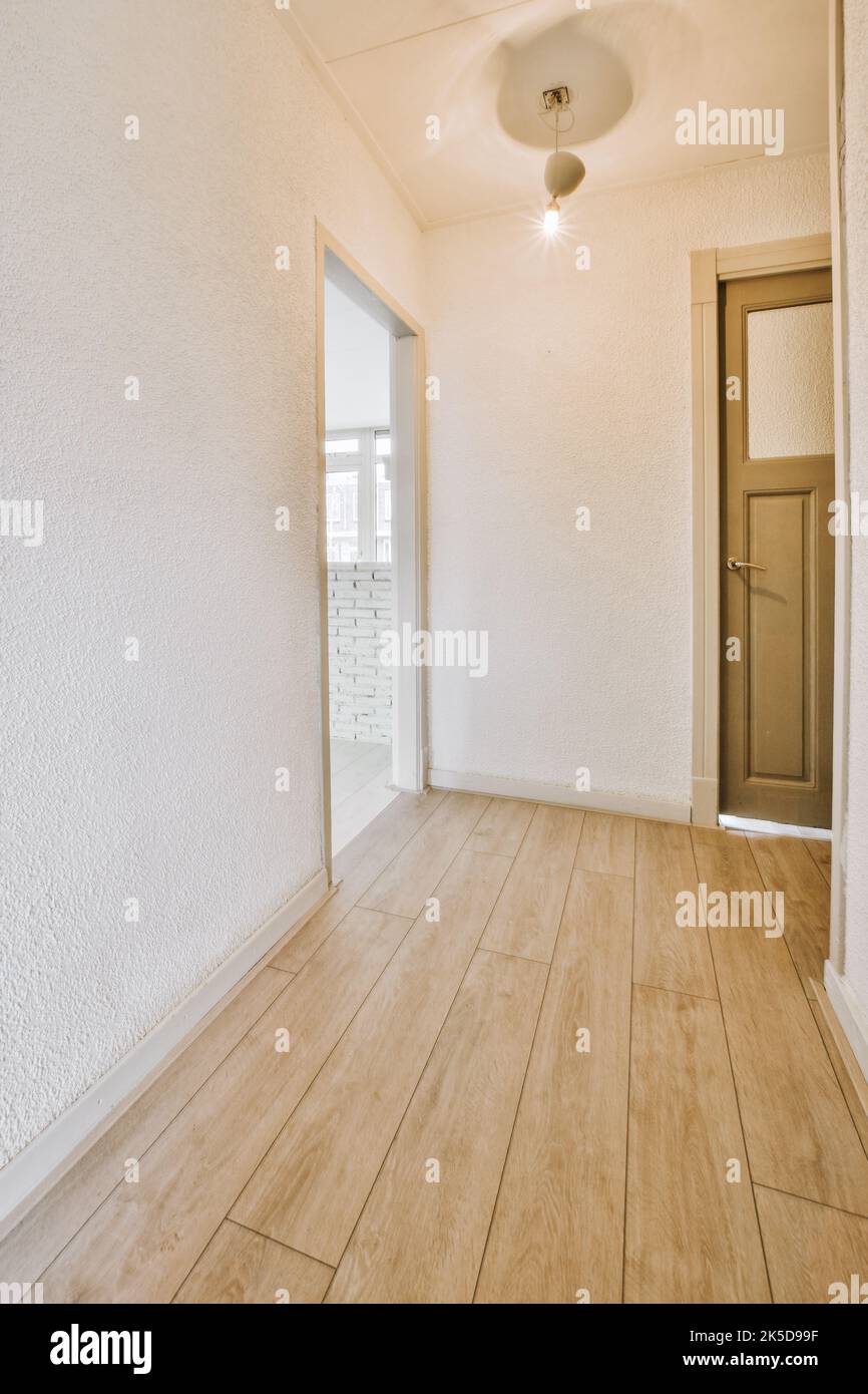 Narrow corridor with white walls and doors leading to spacious room ...