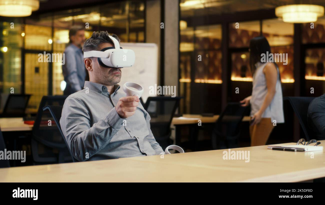 Male office worker wearing VR headset and using wireless controllers ...