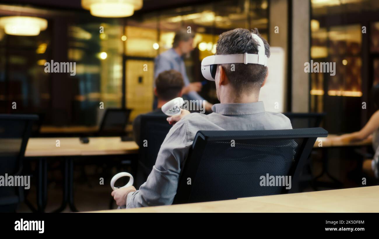 Back view of man wearing VR headset and using wireless controllers ...