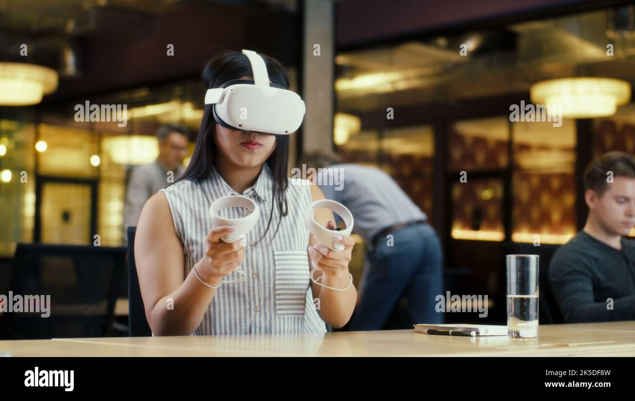Asian female office worker using VR headset and wireless controllers ...