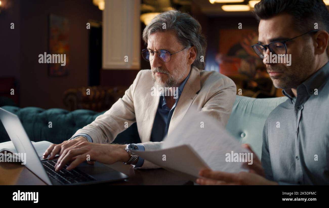 Male colleagues talking, using laptop, working with papers and ...