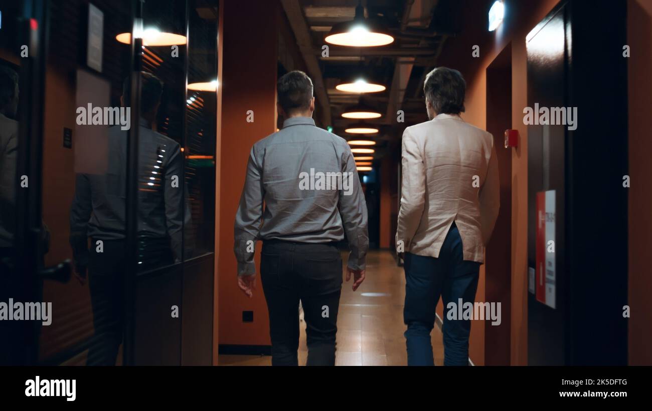 Male colleagues in suits walking down in hallway together, talking ...