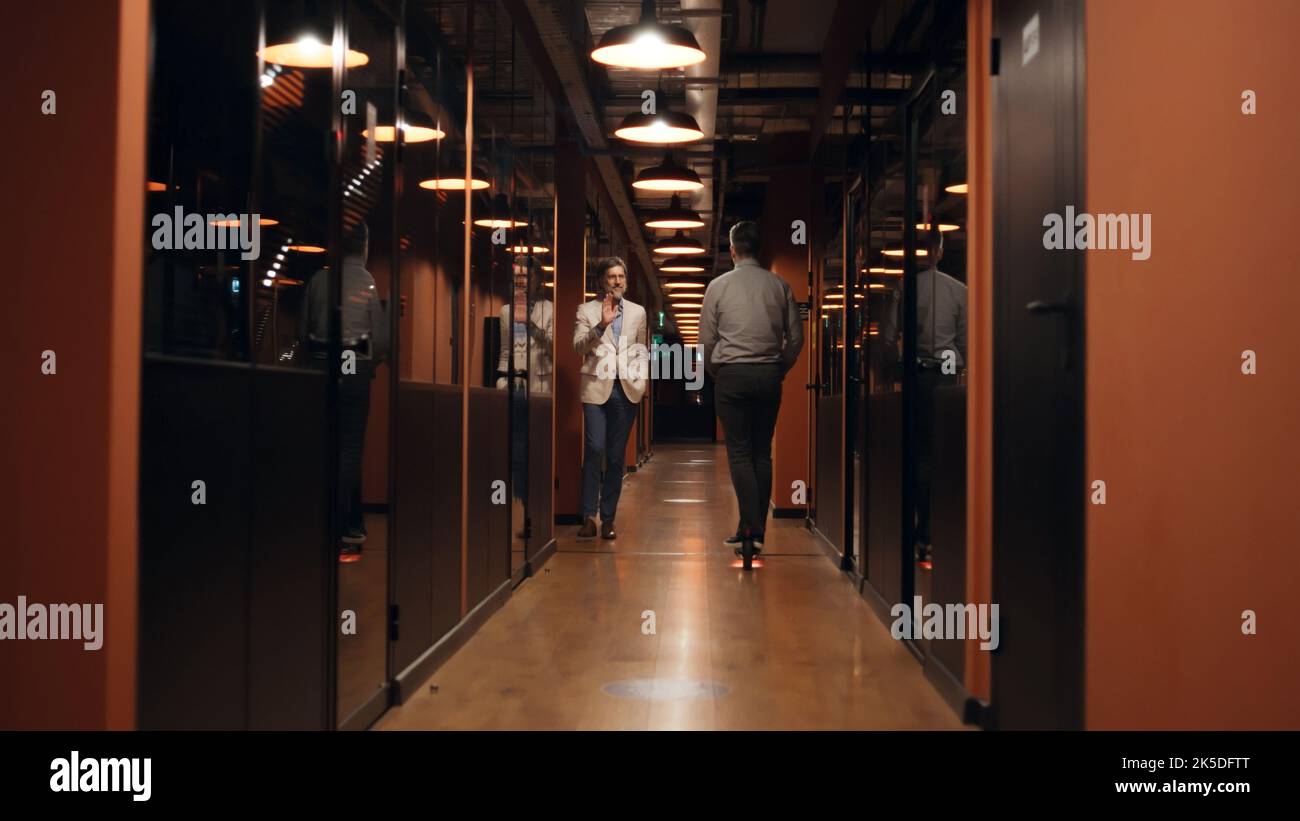 Back view of man riding electric scooter in corridor, meeting and ...
