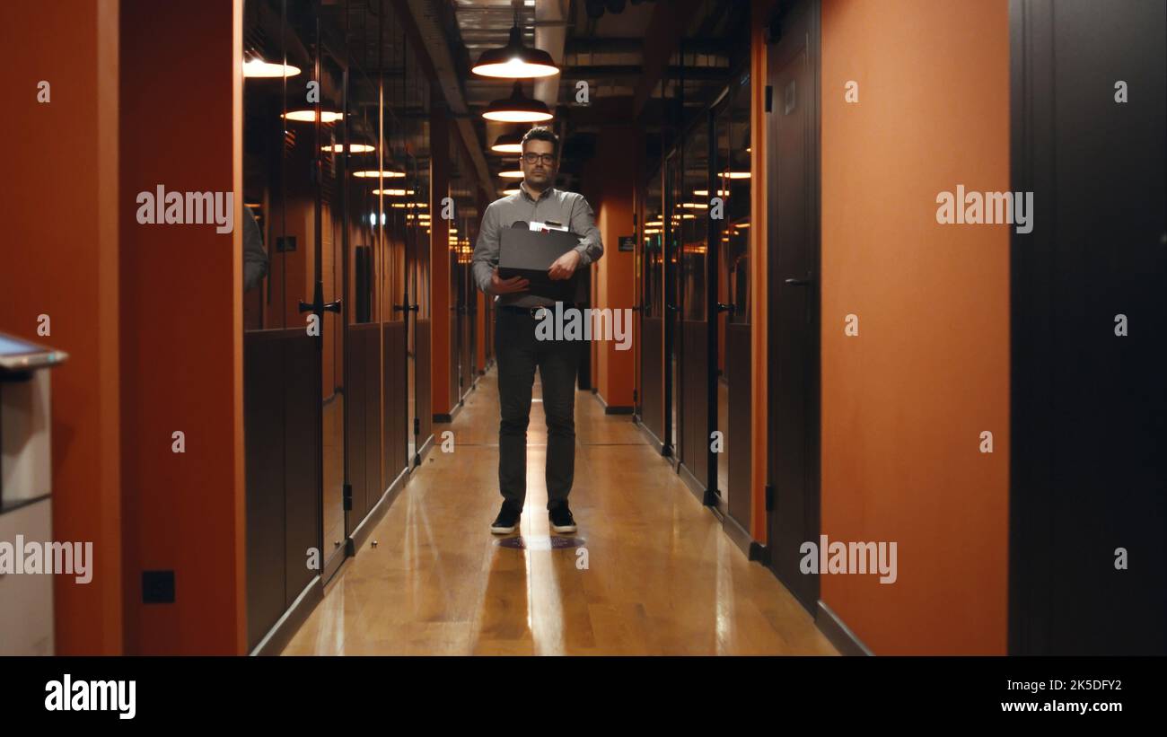Fired upset man in suit walking down in office hallway, holding box ...