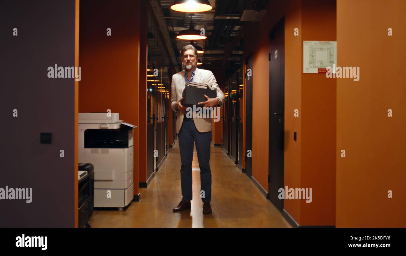 Fired male worker in suit standing in office corridor, holding box with ...
