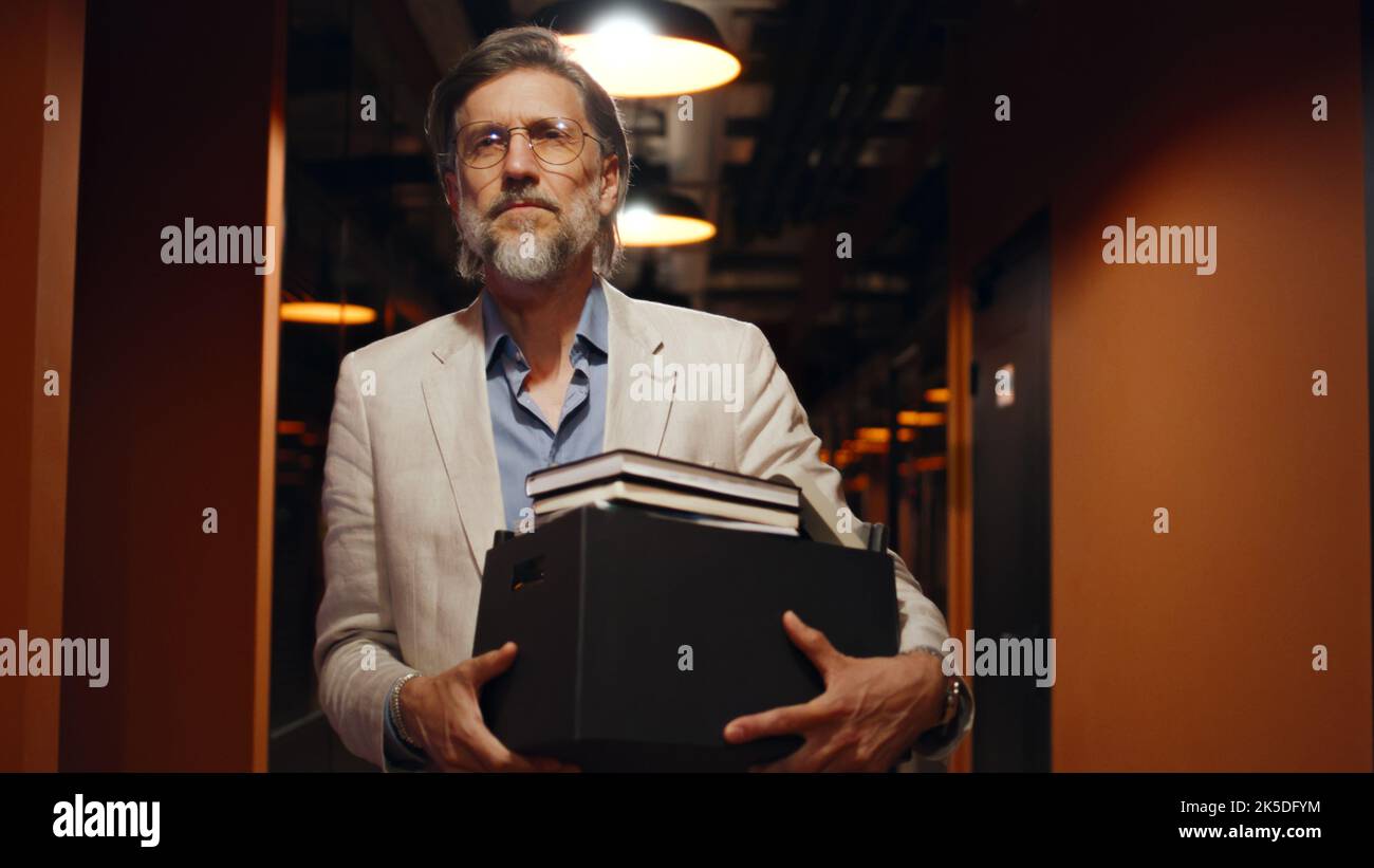 Fired male worker in suit standing in office corridor, holding box with ...