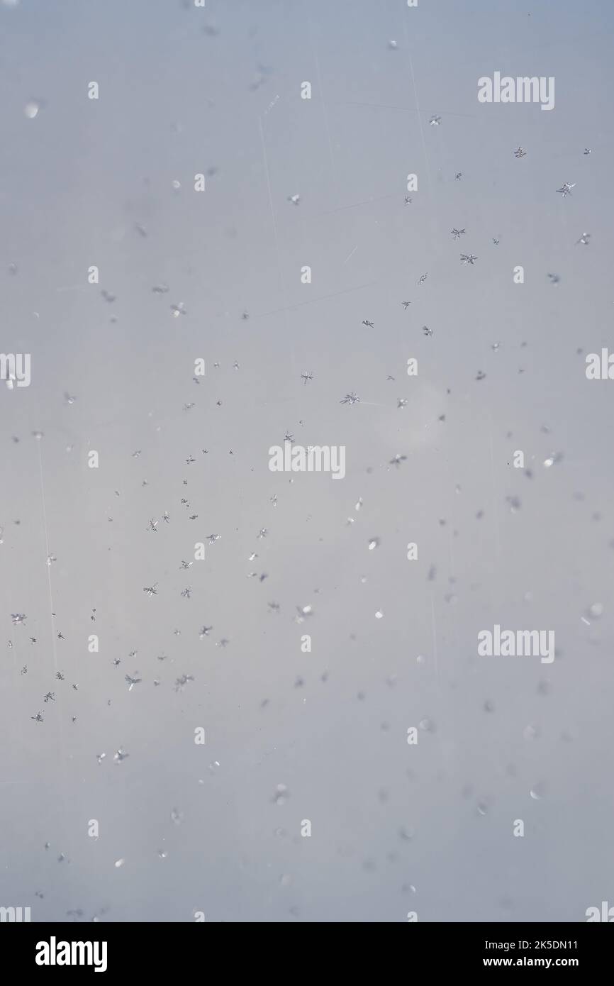 A vertical closeup of a frozen plane window with snowflakes in the ...