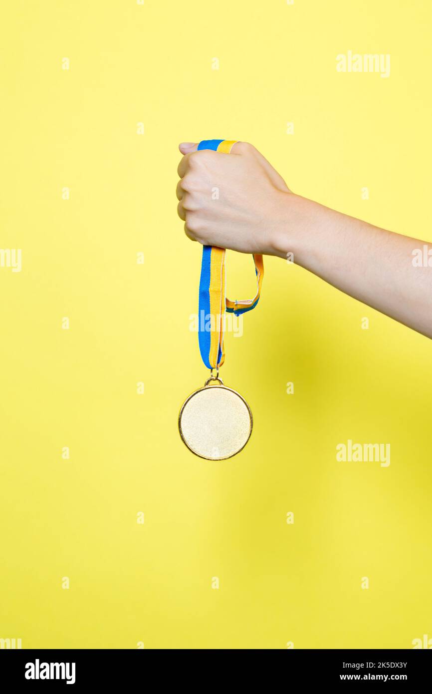 Hand hold Gold medal on yellow blue ribbon isolated on yellow ...