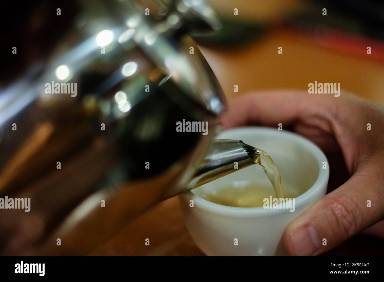 Close up hot tea pouring into a white cup. Blurry lights on black ...