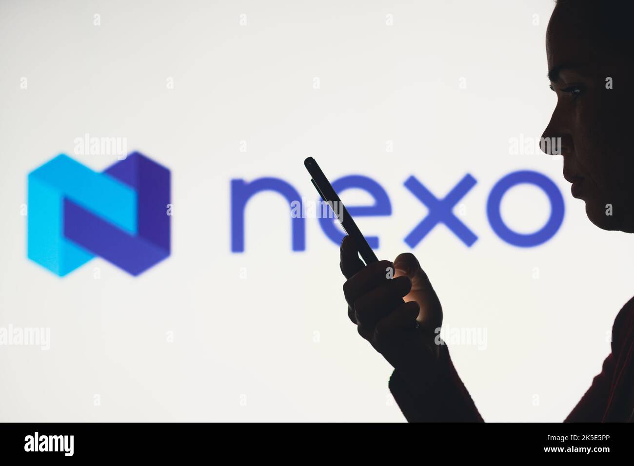 In this photo illustration, a woman's silhouette holds a smartphone with the Nexo (nexo.io) logo ...
