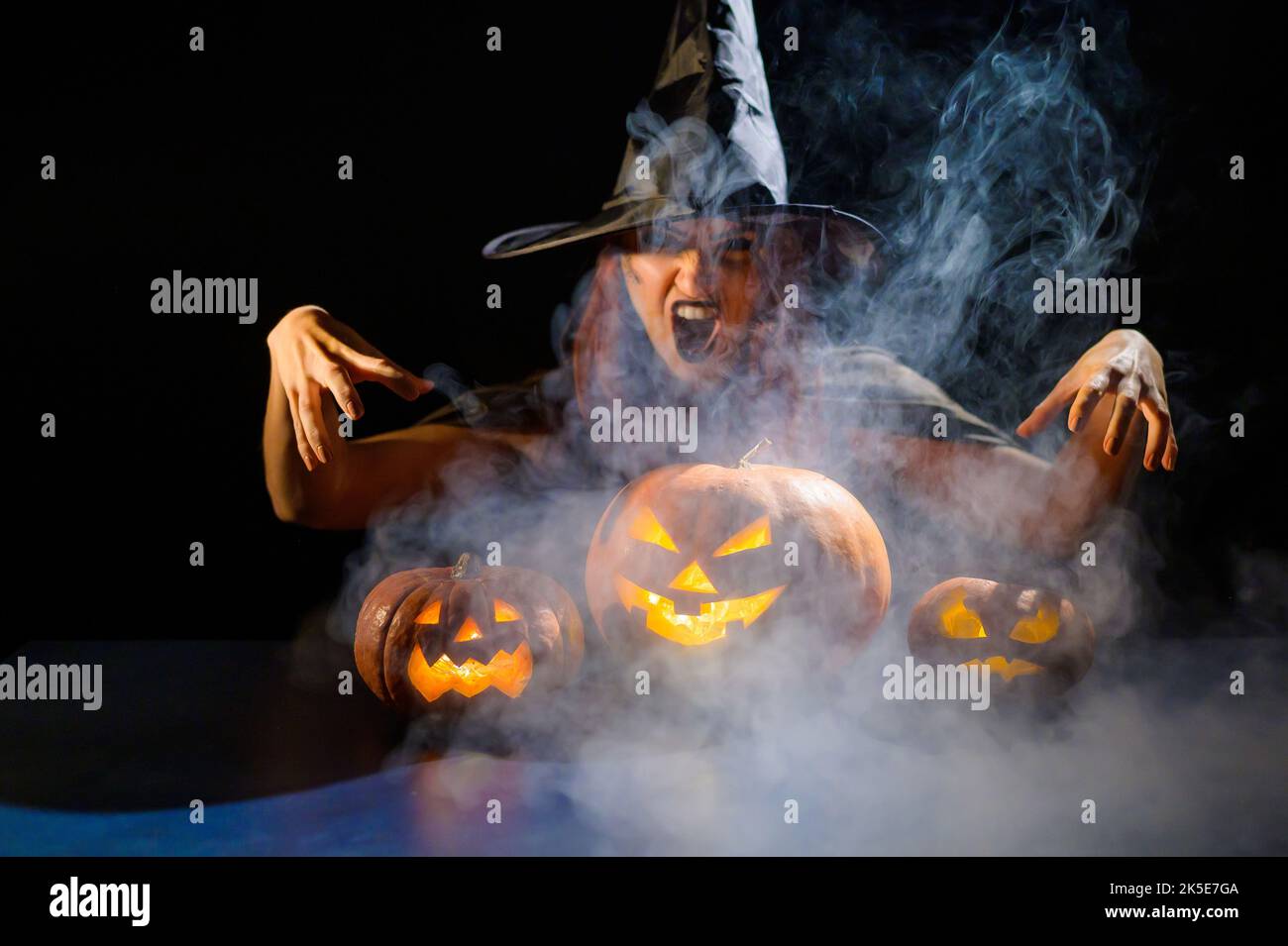 An ominous witch in a hat conjures over a jack-o-lantern. Traditional ...
