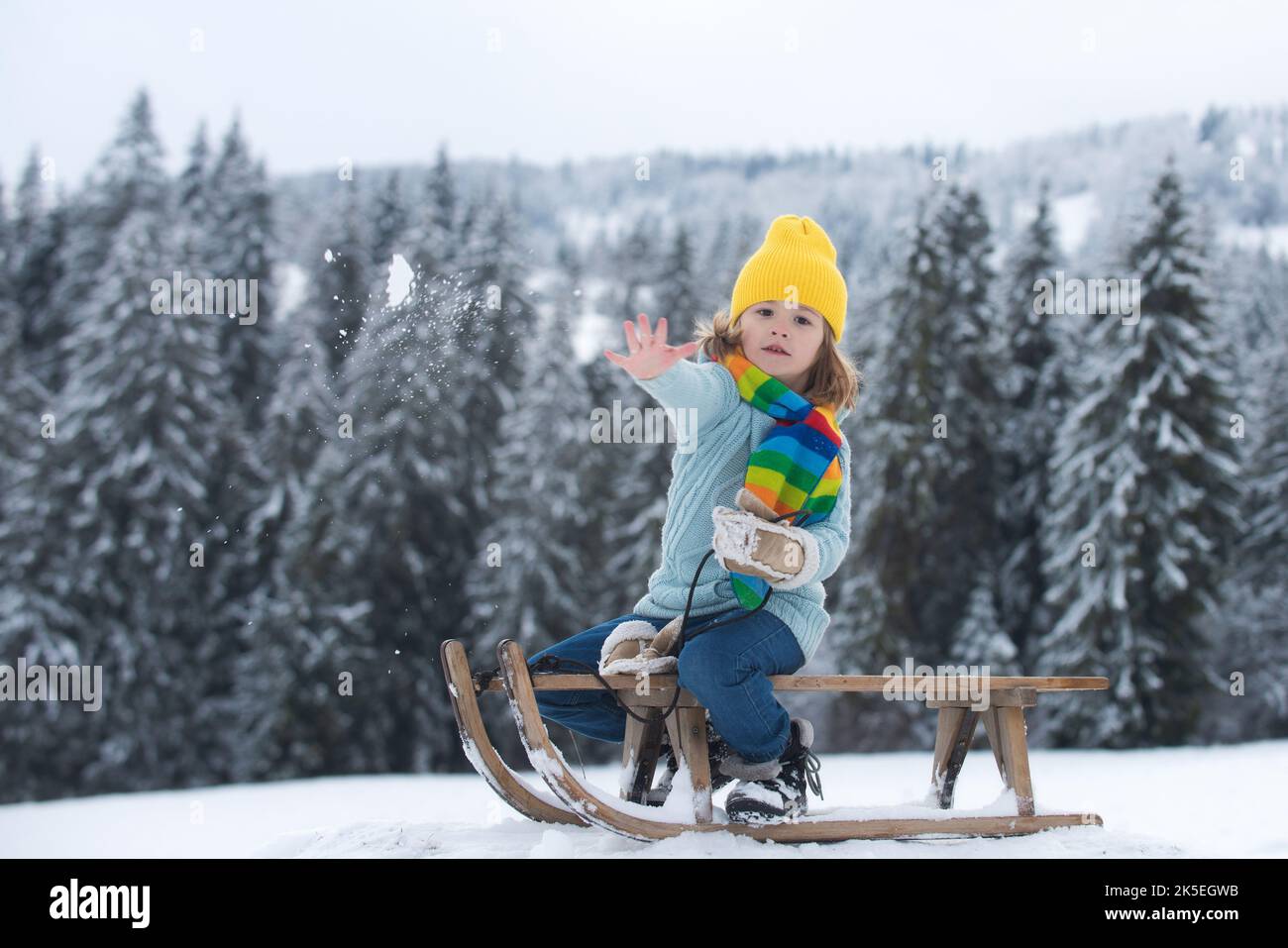 Child boy sledding in winter, playing with snowball. Kid riding on snow ...