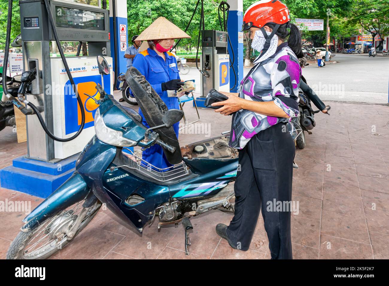 Petrol filling station attendant wearing uniform and bamboo hat filling ...