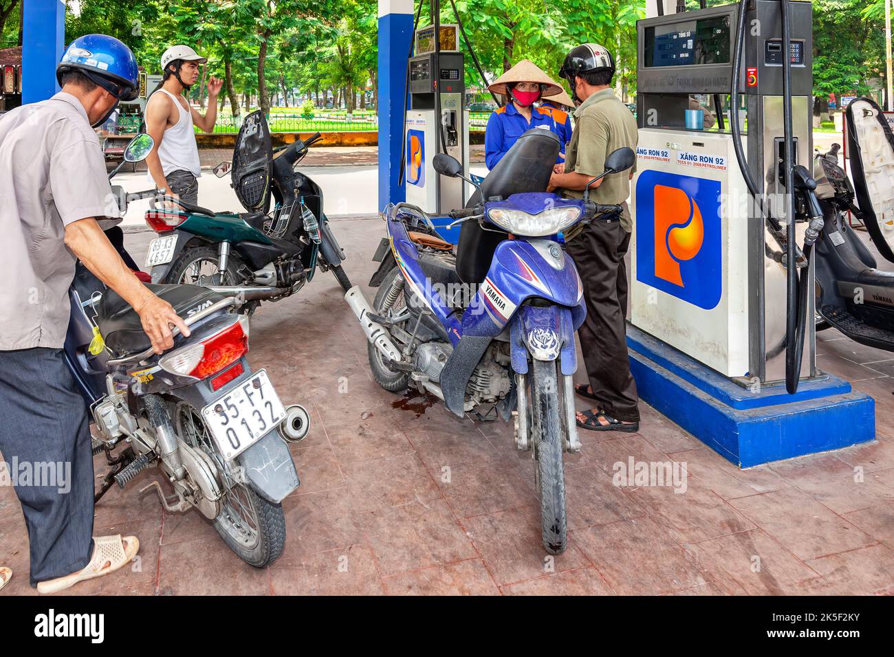Petrol filling station attendant wearing uniform and bamboo hat filling ...