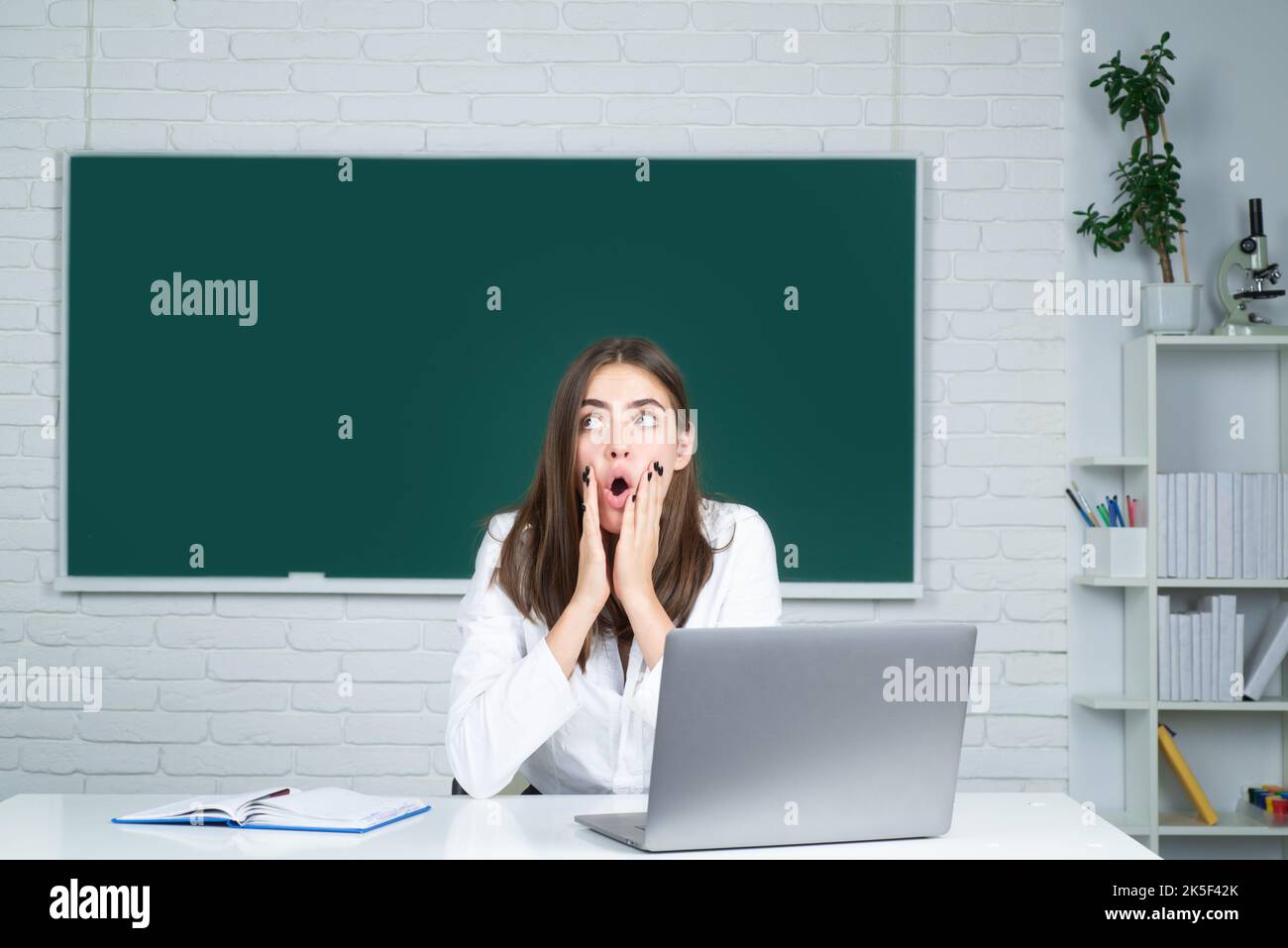 Portrait of a surprised female student studying in school classroom ...
