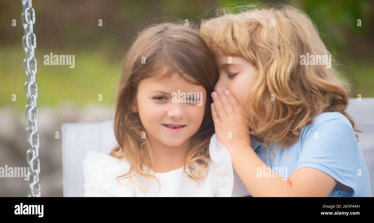 Little boy whispers to lovely girl in ear. Two children outdoors ...