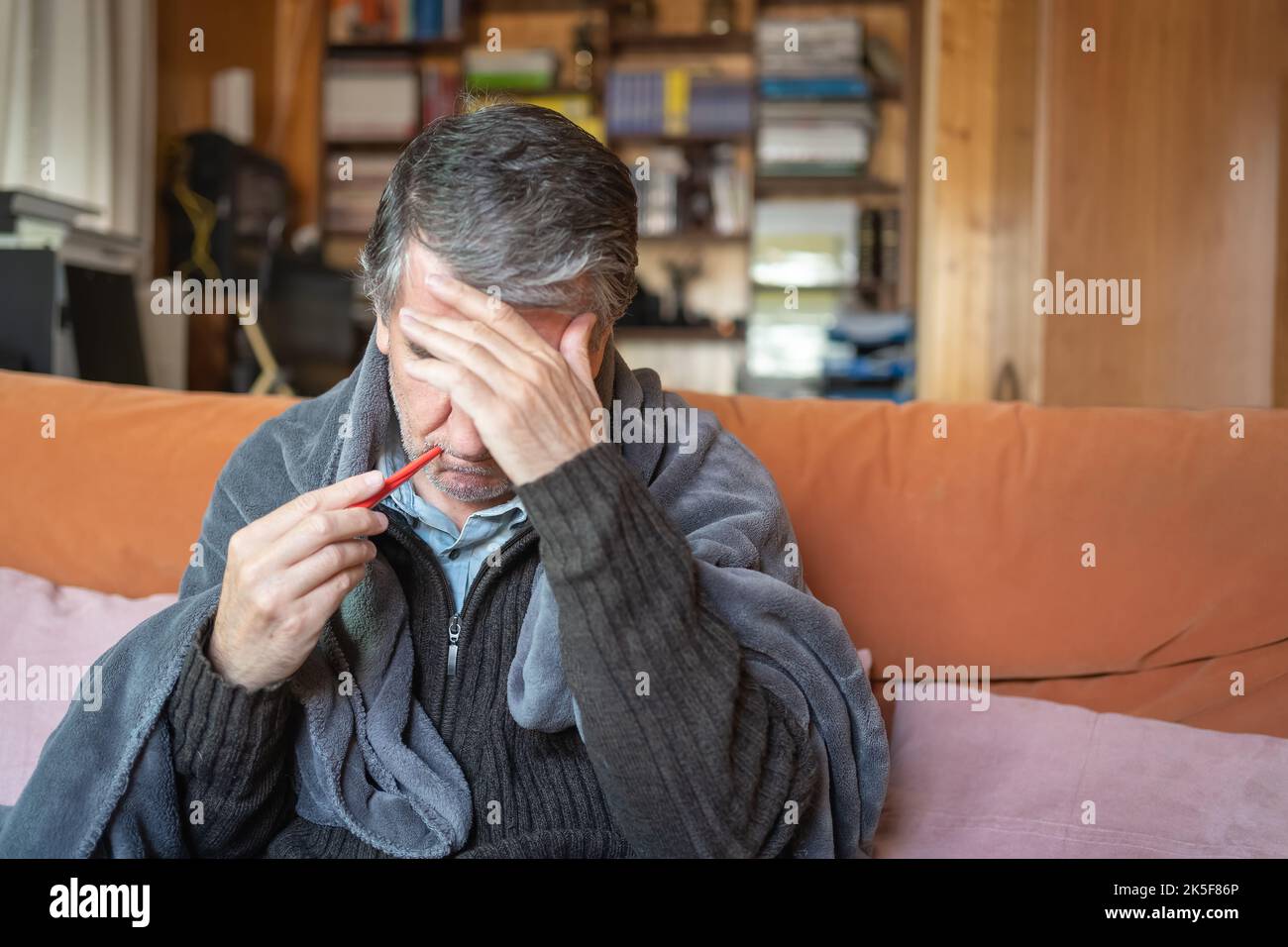 Sick and cold man at home, taking his temperature with a thermometer in ...