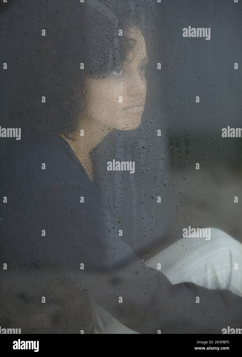 THe dark side of depression. A sad young woman looking out at the rain ...