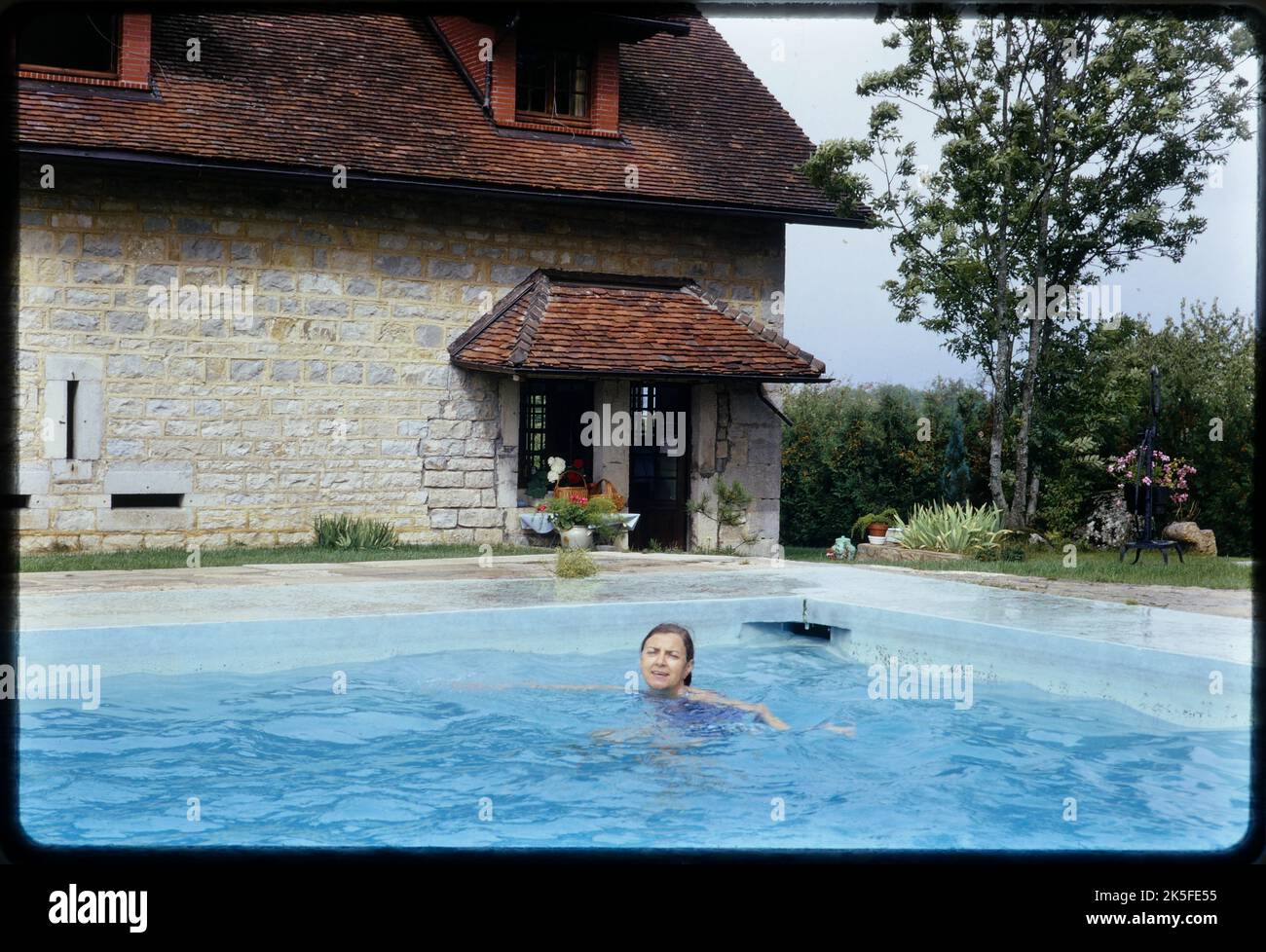 Middle-aged woman bathing in the swimming-pool of a country house ...