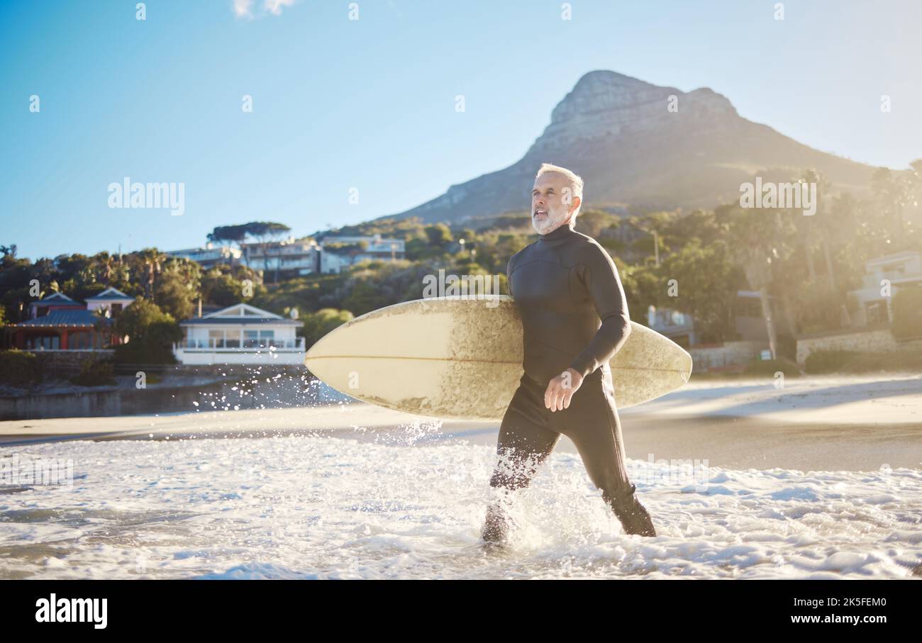 Beach, surfing and senior man with a surfboard walking in the ocean ...