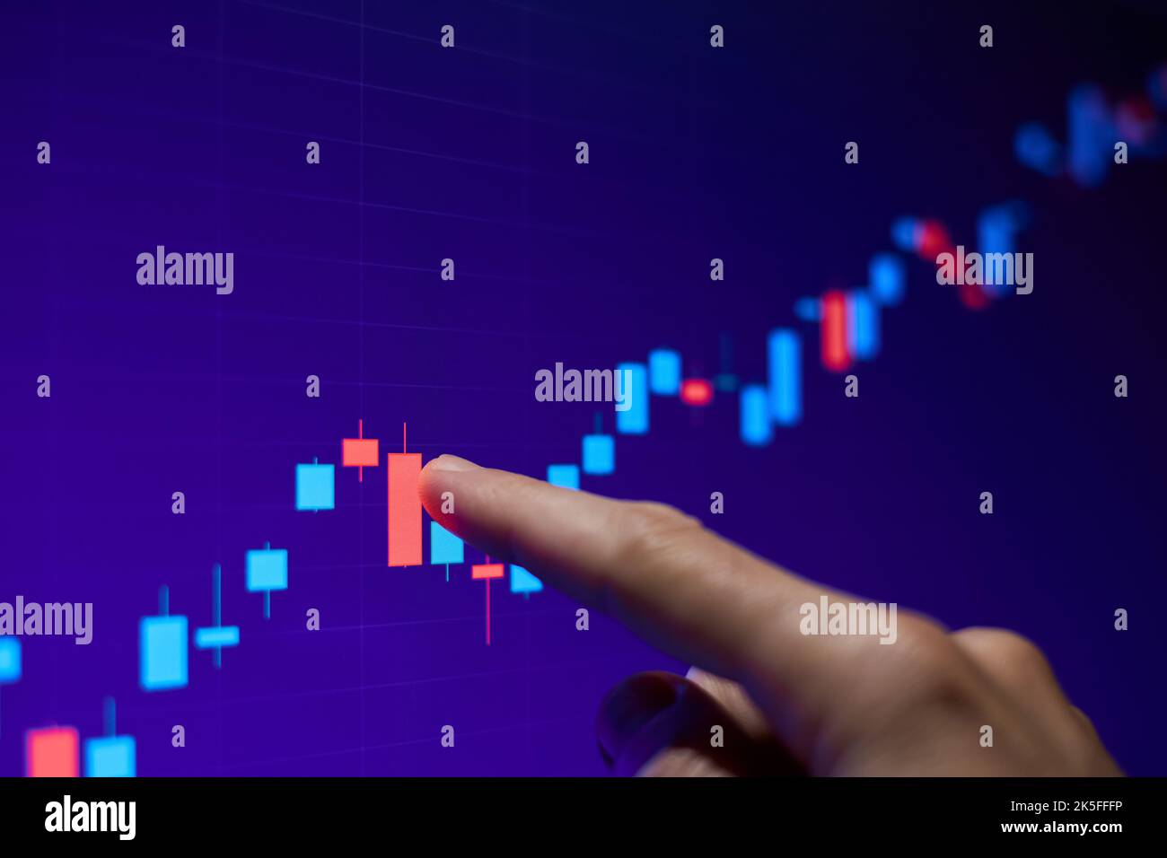 The trader points his finger at the Rising stock chart on the monitor ...