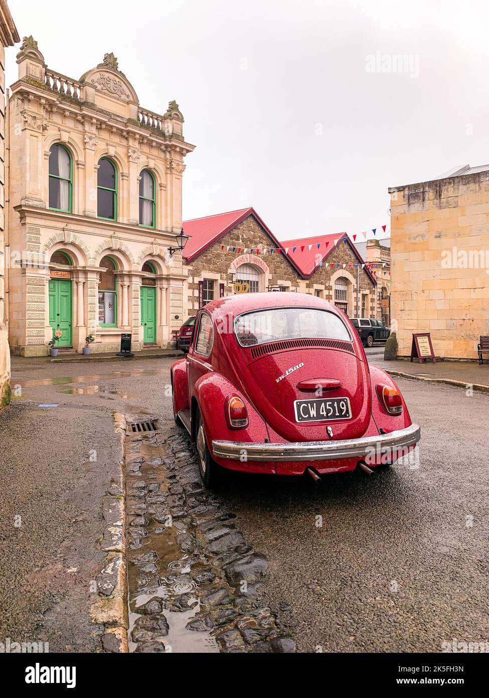 A red classic old car parked on the rainy street in Oamaru in a ...