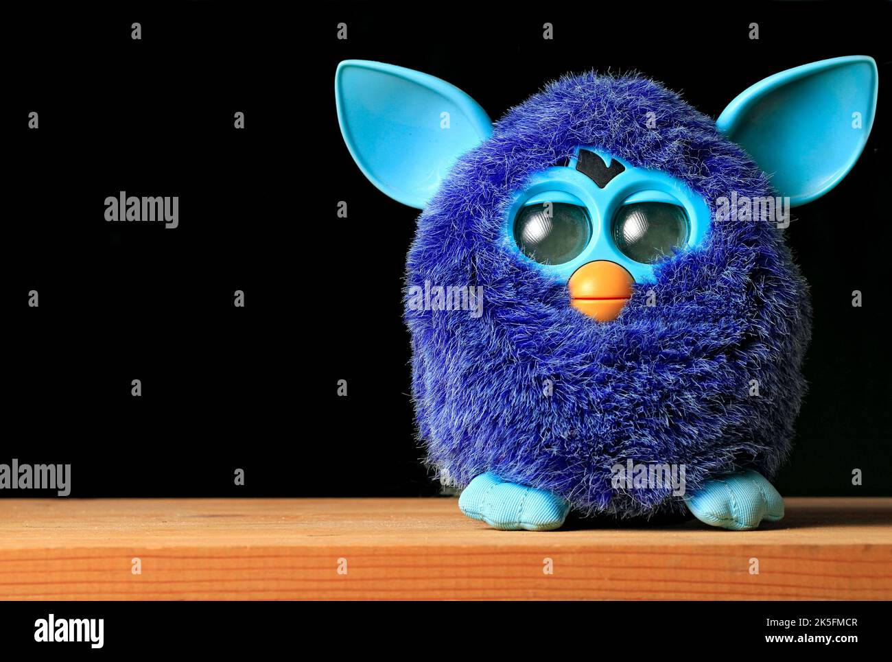 Electronic robotic Furby toy sitting on wood on a black background ...