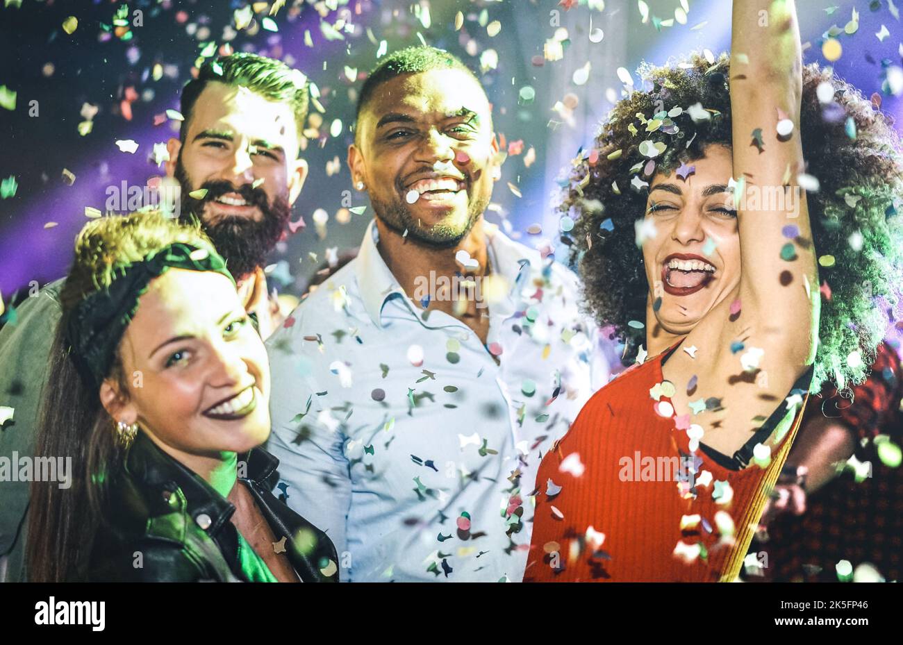 Multiracial young friends dancing at night club under confetti rain ...