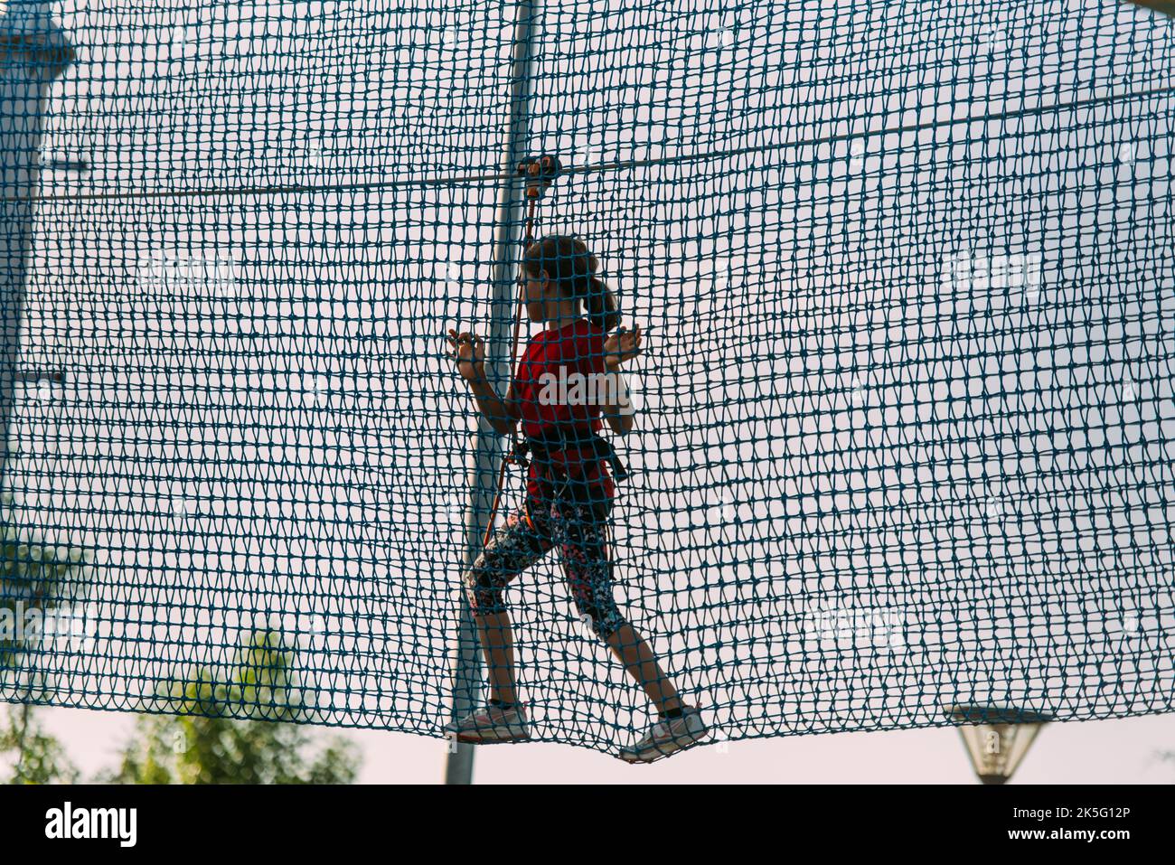 Young kid making her way through the net bridge in the adventure park ...