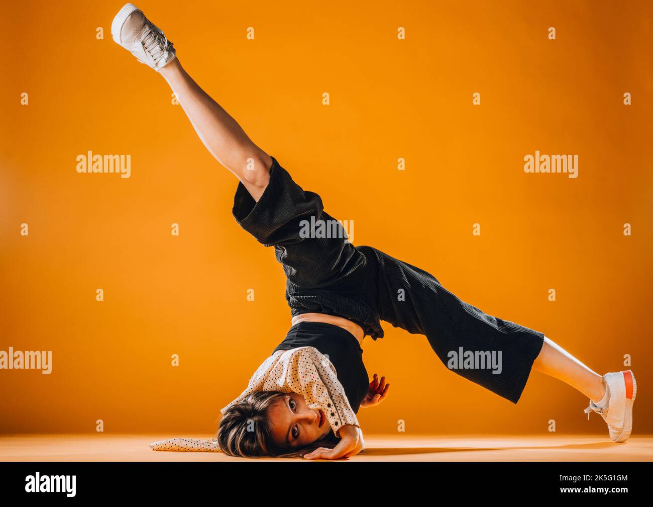 Fit young girl dancer performing a dance routine in the orange studio ...