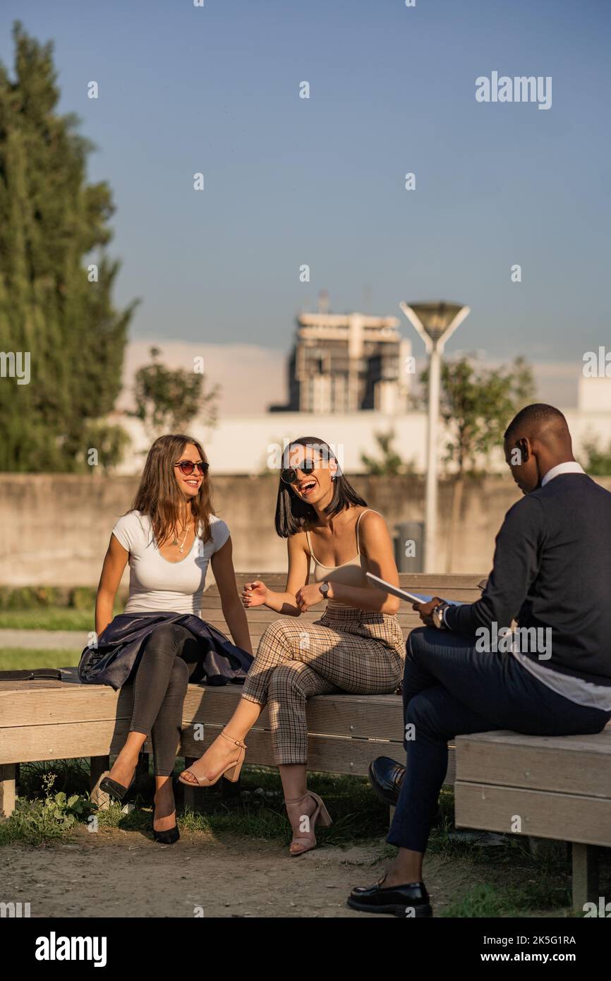 Three multiracial business people are laughing together while sitting on the bench Stock Photo ...