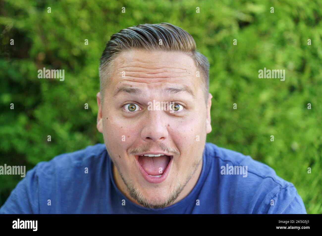 Young man gawping at the camera with mouth open and wide surprised eyes ...