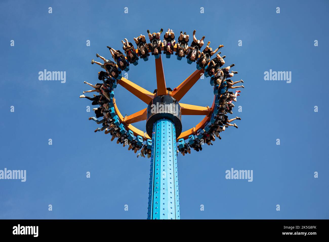 People hanging upside down against blue sky at X amusement ride in ...
