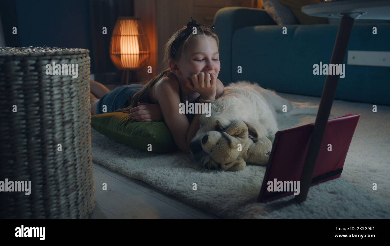 Girl lying on mild carpet with dog, watching funny movies on digital ...