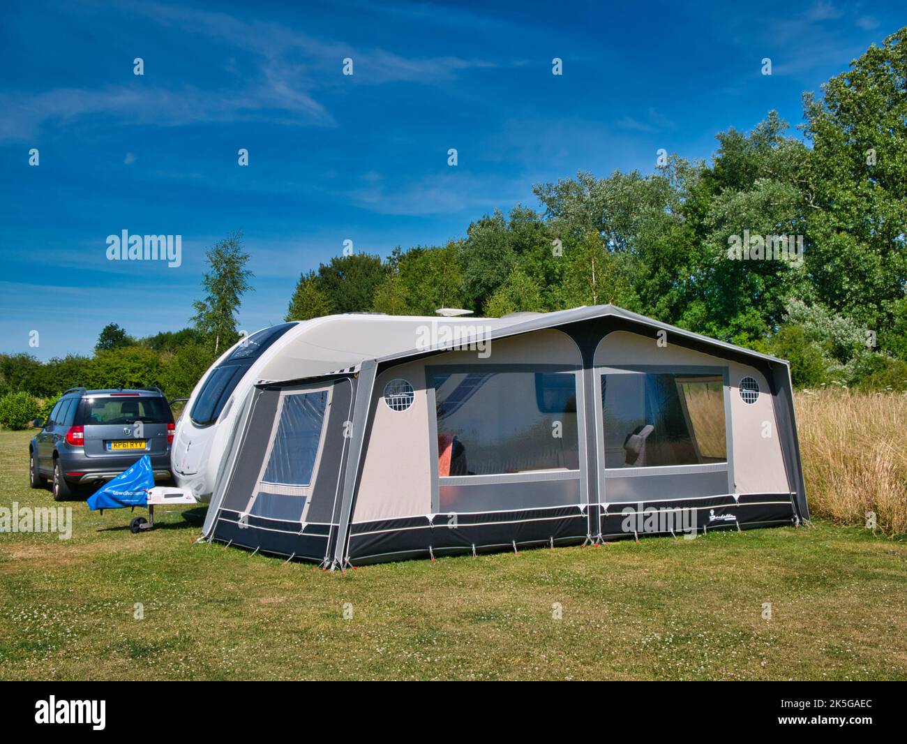 Pitched in a grassy field, a white caravan with full awning and car on ...