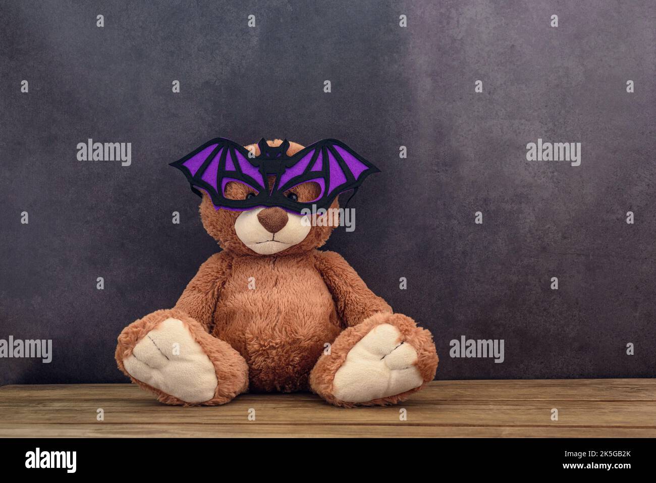 Funny brown teddy bear with purple bat shaped mask sits on old wood ...