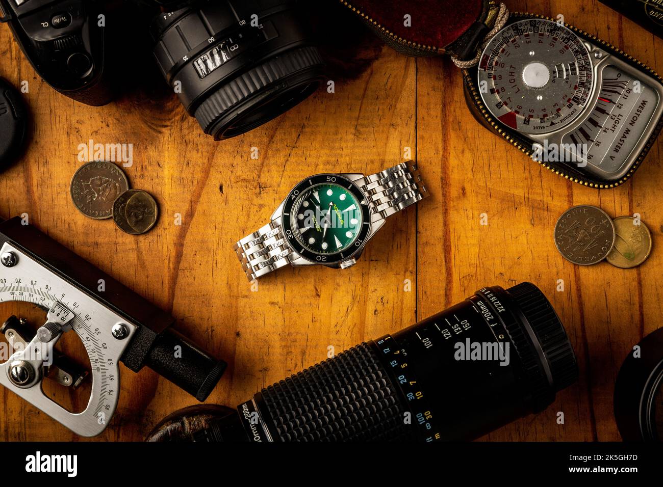 A top view shot of a silver and green watch sitting amongst old camera ...