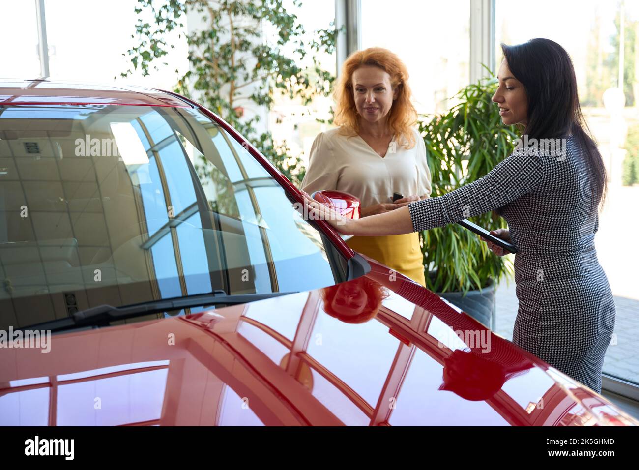 Two women inspecting selected car model in a car dealership Stock Photo ...