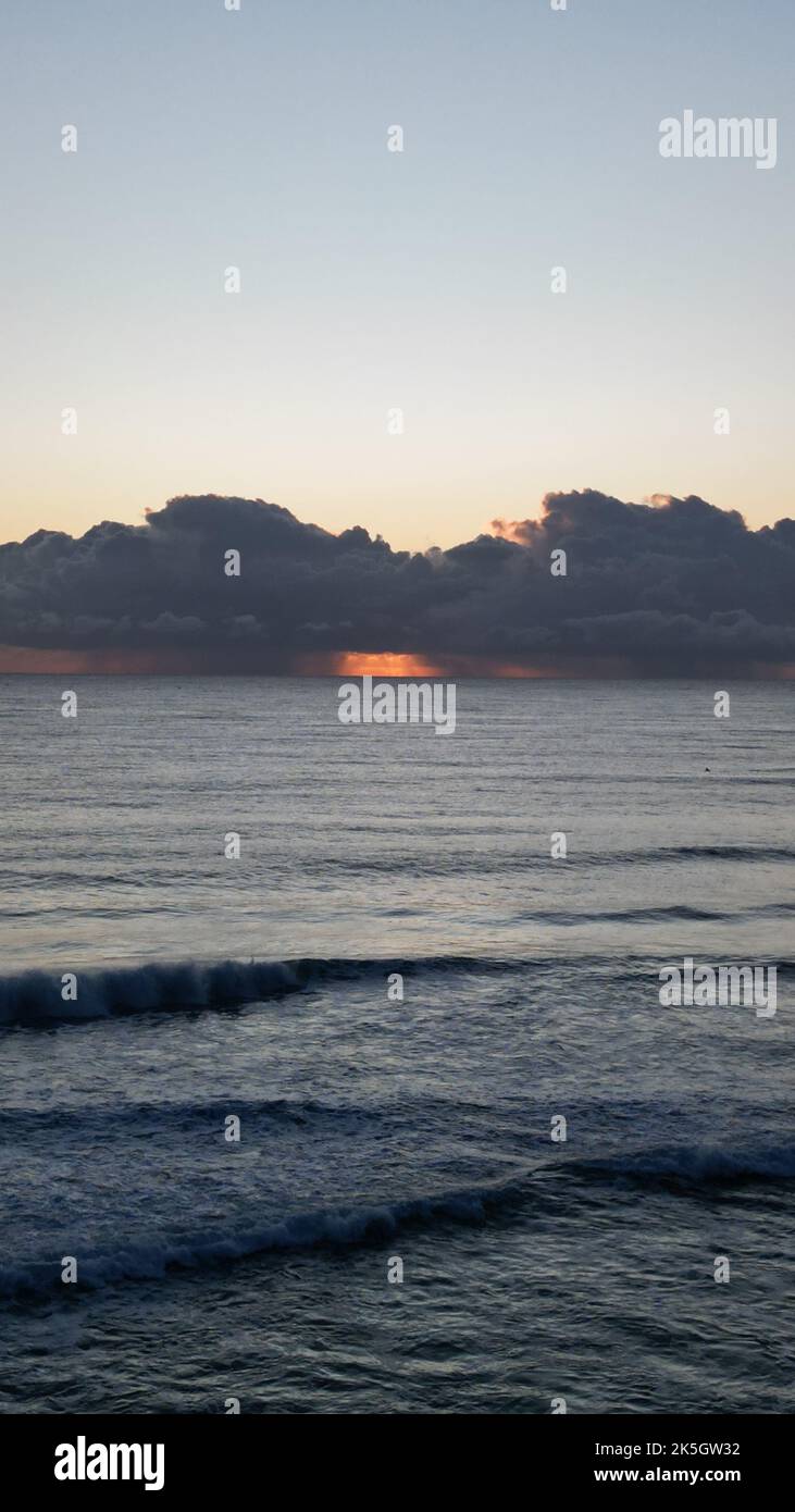 A vertical shot of a beautiful seascape with a sunset hiding behind the ...