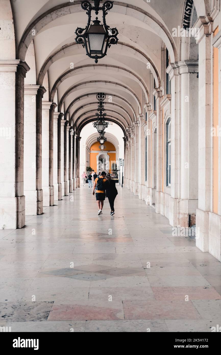 A couple walking on a path under a white stone arched column building ...