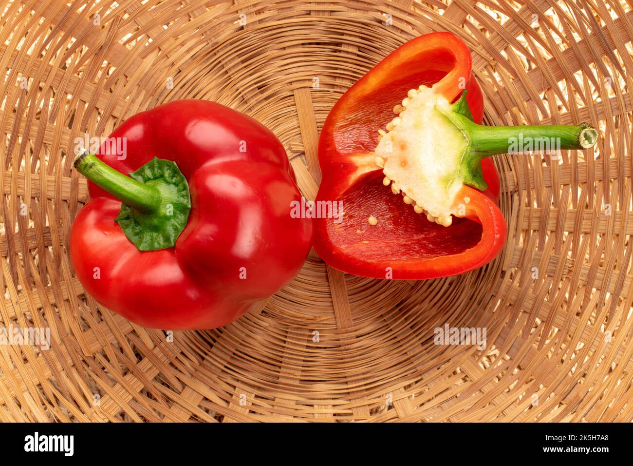 One whole and one half red bell pepper, close-up, in a straw dish, top ...