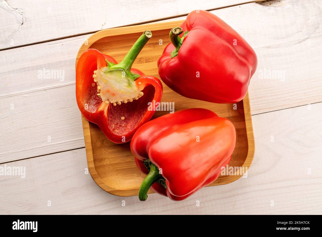 Two whole and one half red bell peppers on a bamboo plate, close-up, on ...