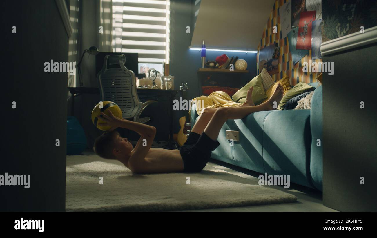 Young boy do abs crunches while holding football in his hands and legs ...