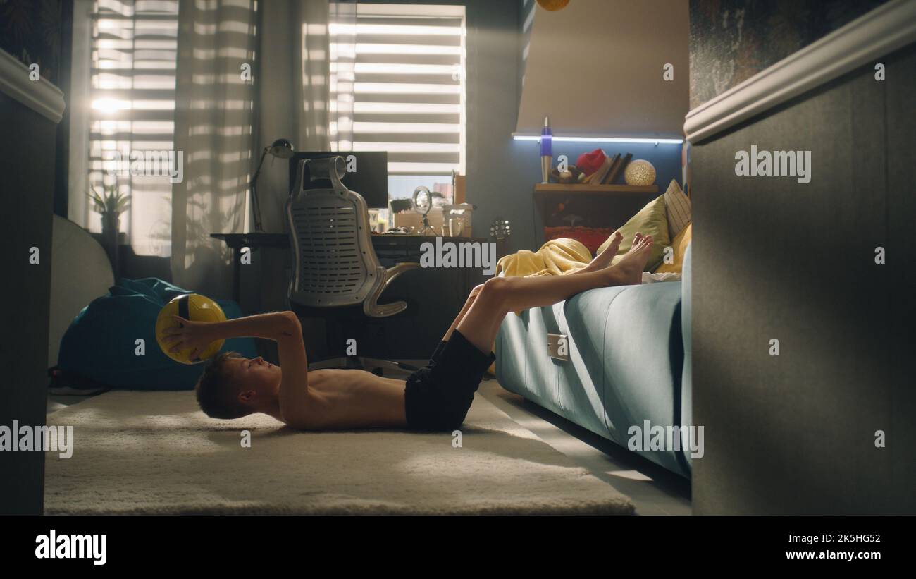 Young boy do abs crunches while holding football in his hands and legs ...