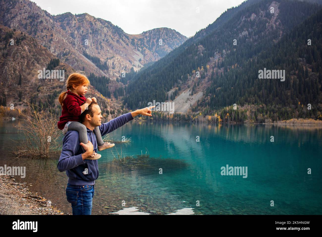 my daughter is around my dad's neck on a mountain lake. dad shows his ...