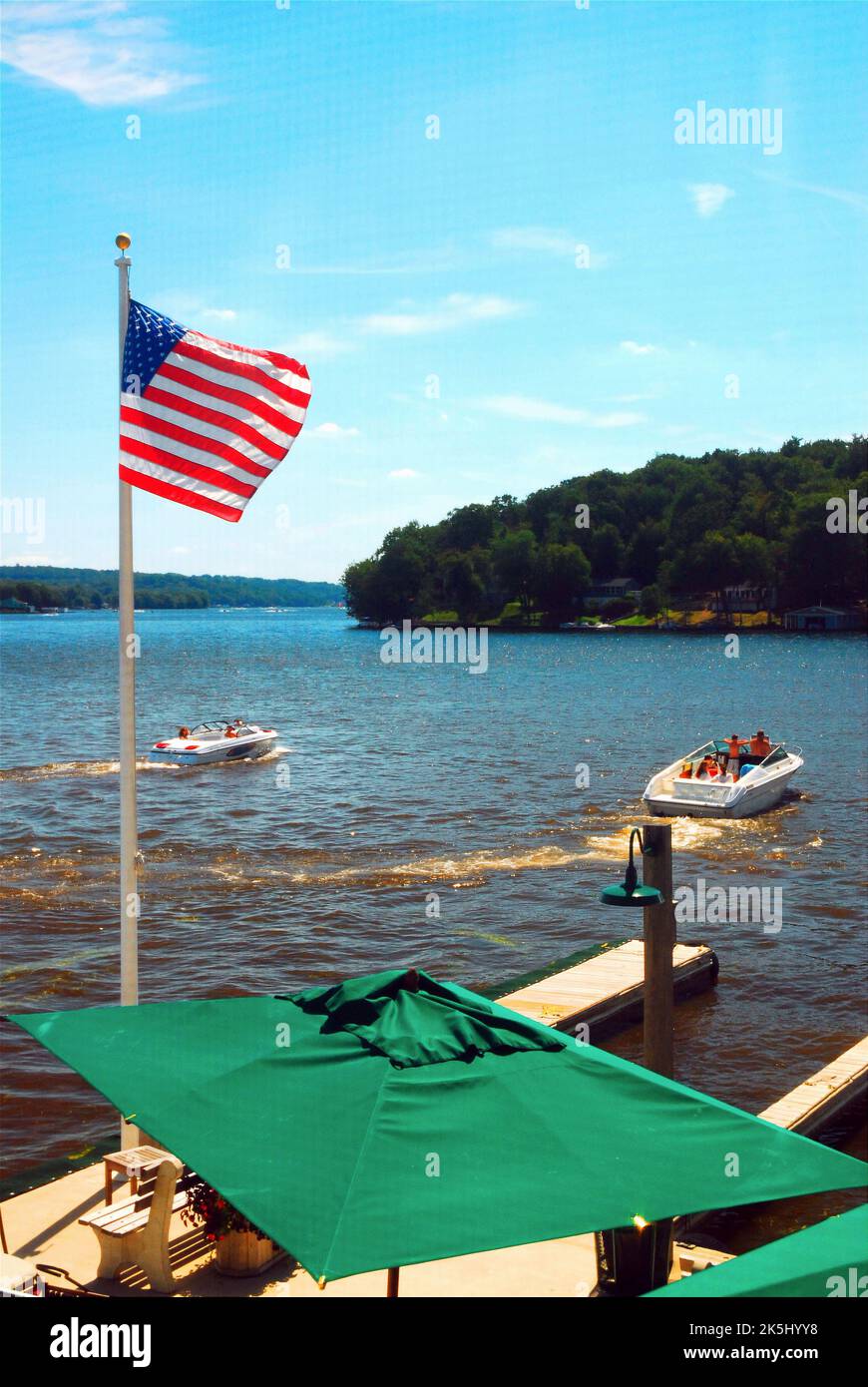 Small boats cruise the lake near a waterside cafe on a sunny summer ...