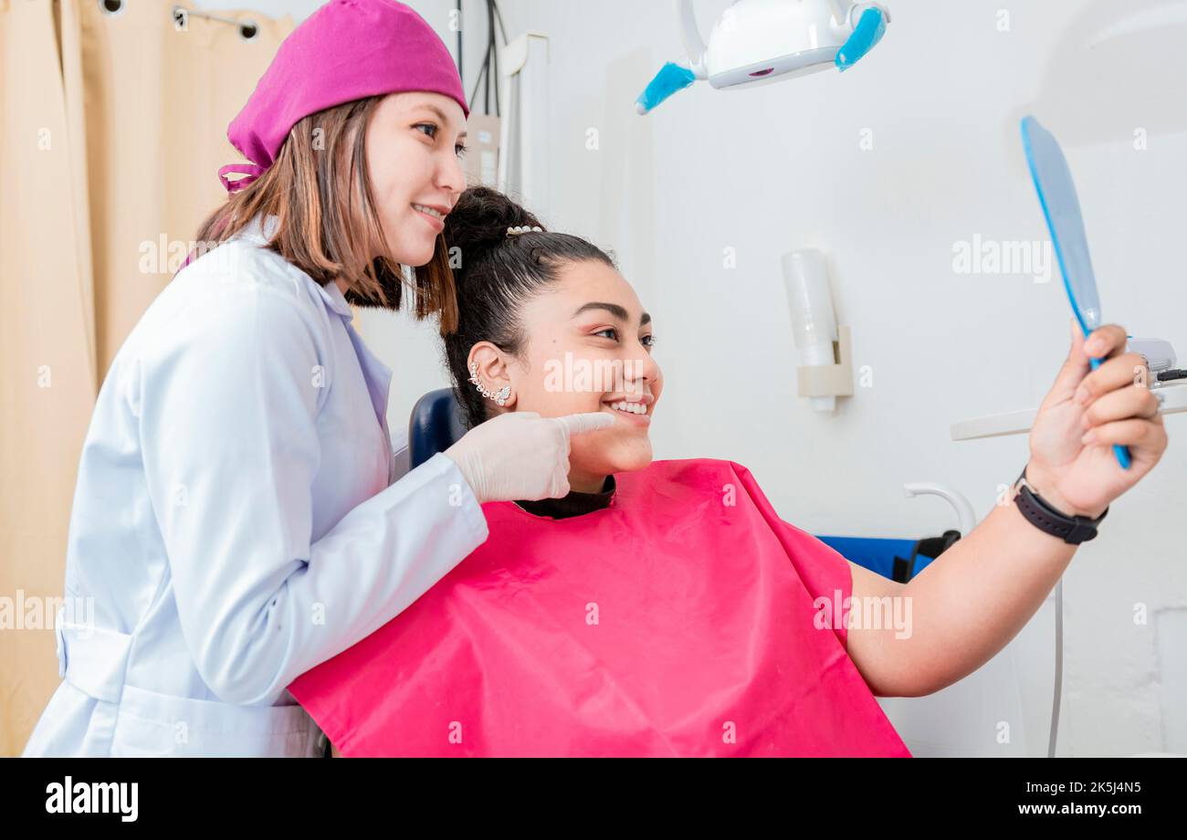 Female patient checking teeth after curing teeth in dental clinic. Dentist with satisfied ...