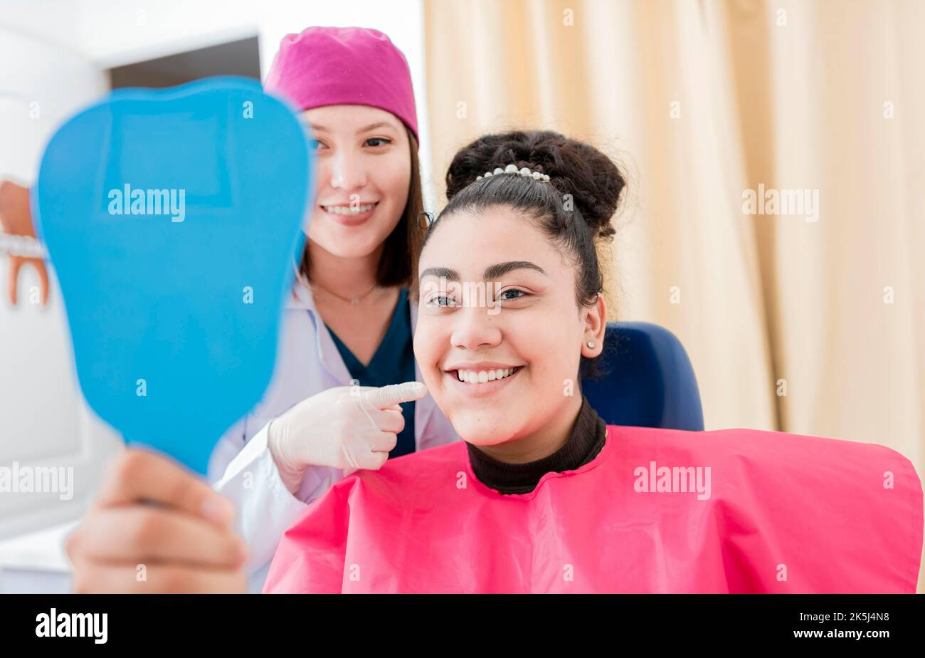 Satisfied patient in dental clinic looking at mirror, dentist next to satisfied patient smiling ...